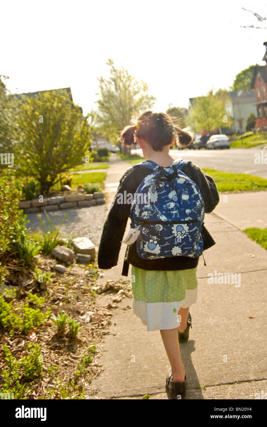 Young girl walking to school wearing a backpack Stock Photo - Alamy