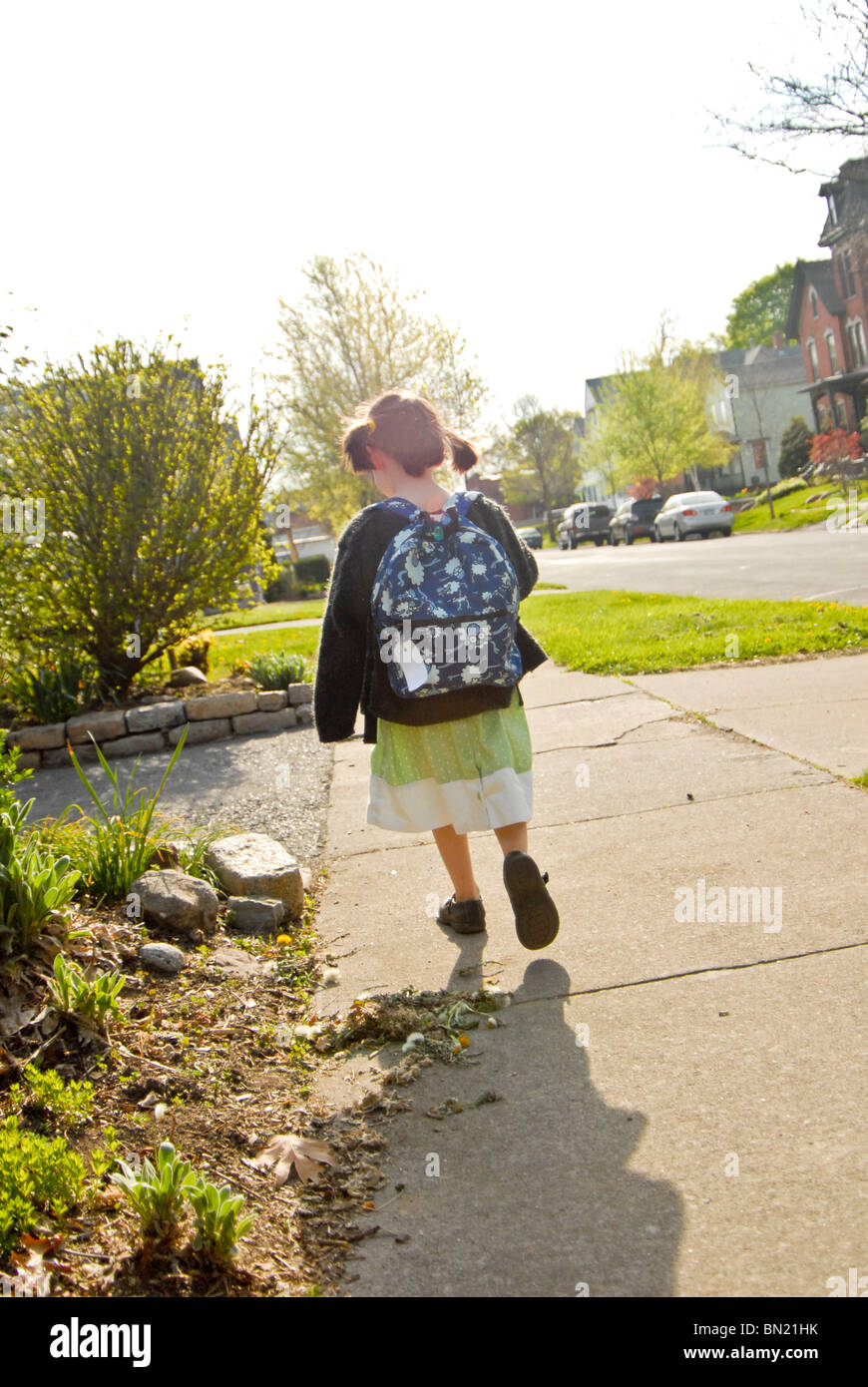 Young girl walking to school wearing a backpack Stock Photo - Alamy