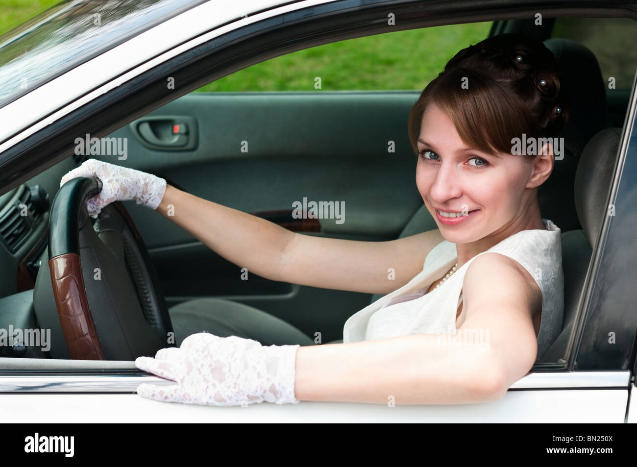 Woman in white dress and white-gloved sitting in car as a driver ...