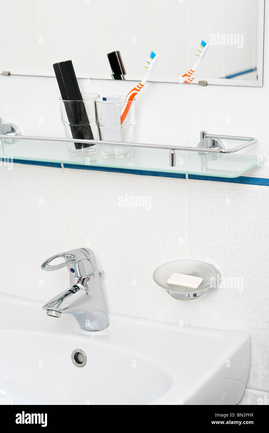 Bathroom accessories: tooth paste and brush on glass shelf. Faucet in ...