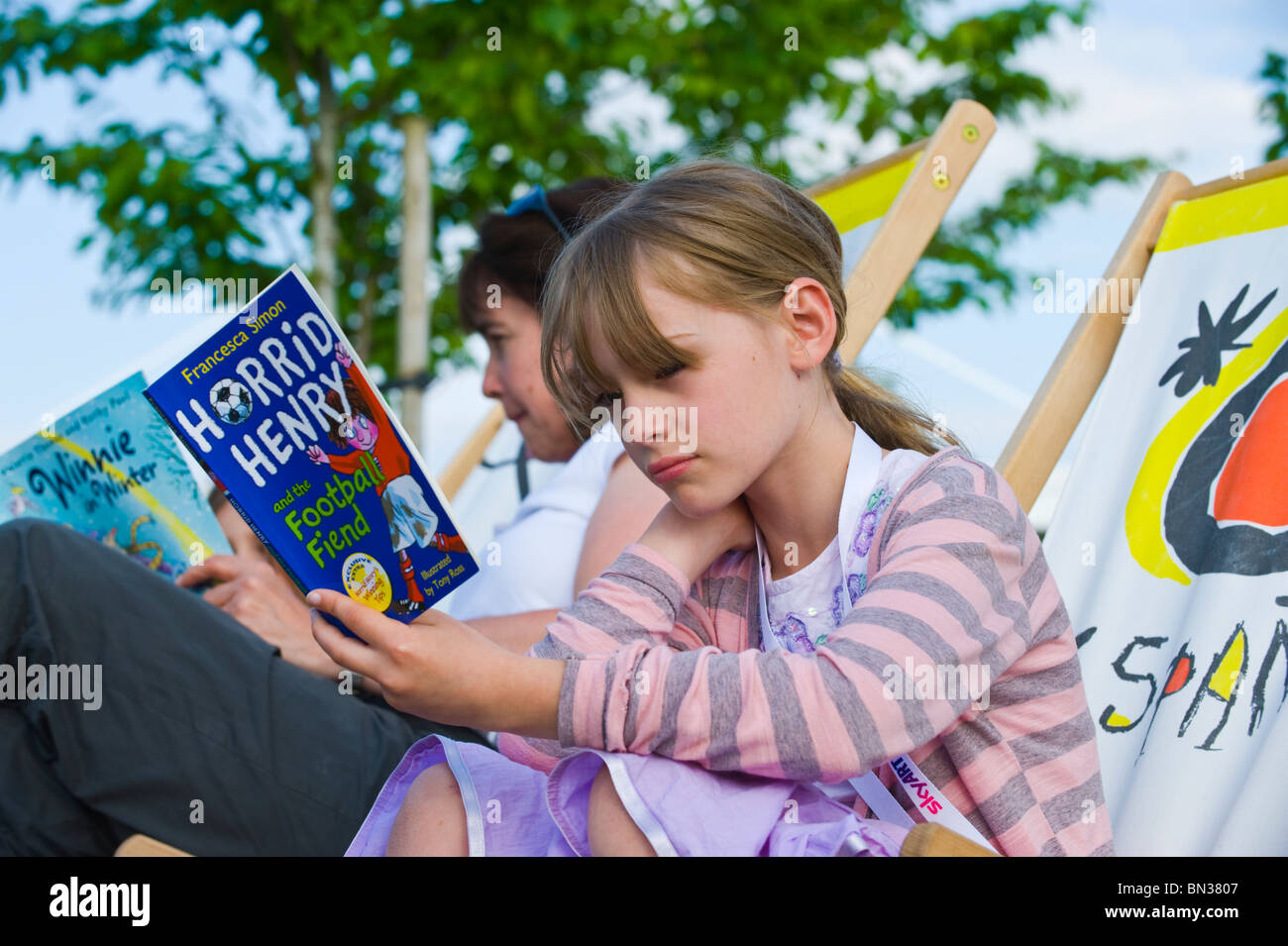 child reading book. Child sat in deckchairs reading in the summer ...