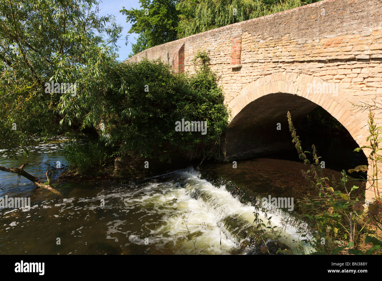 Fast flowing water over a weir under the Harrold road bridge ...