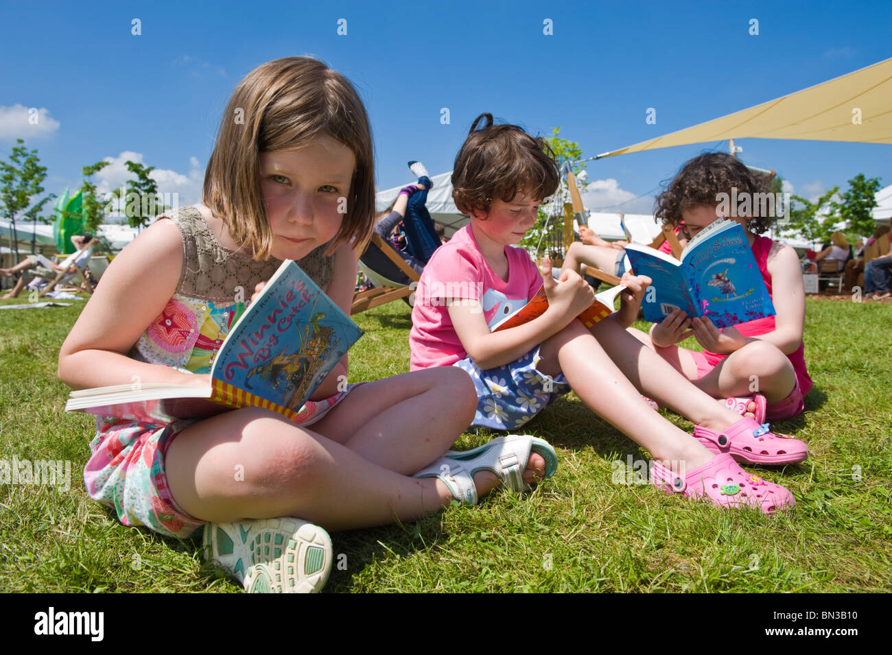 Three young girls sitting on the grass reading books in the summer ...