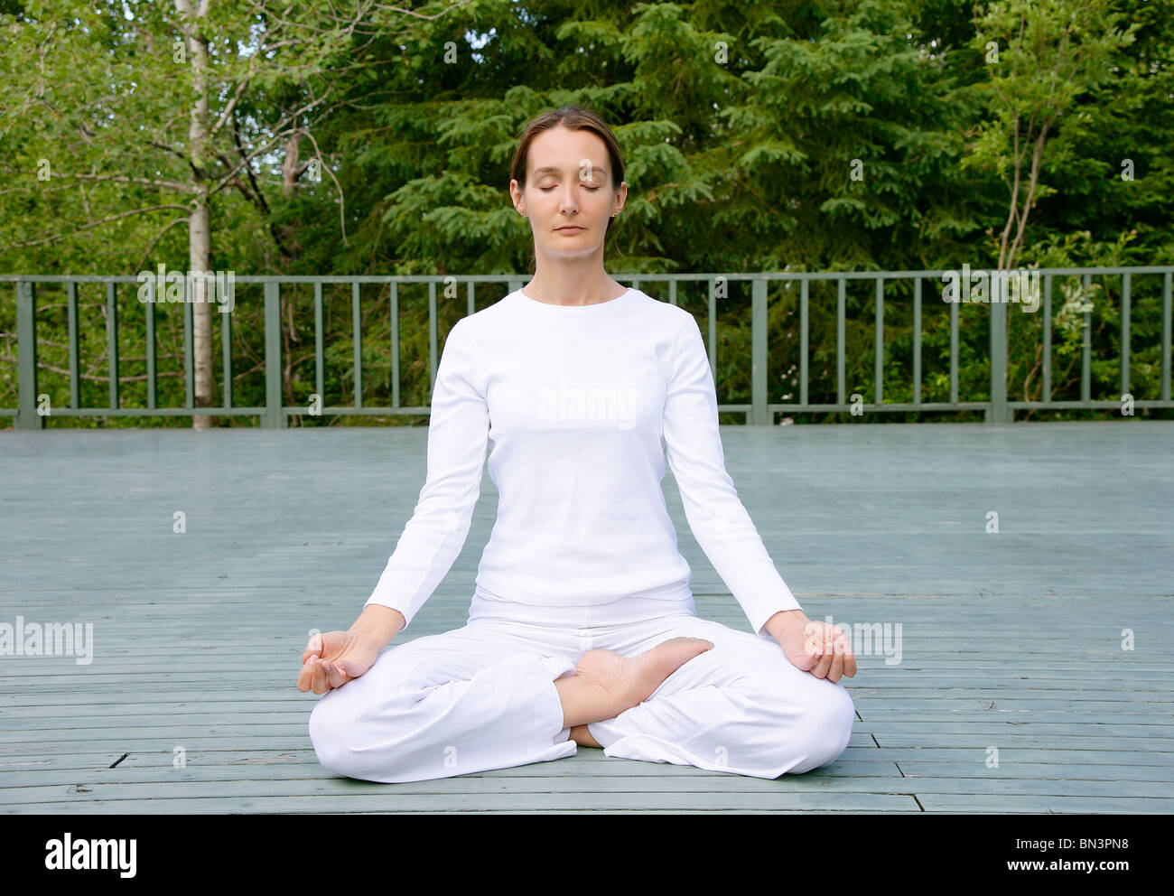 Woman sitting in lotus position on a deck, front view Stock Photo - Alamy