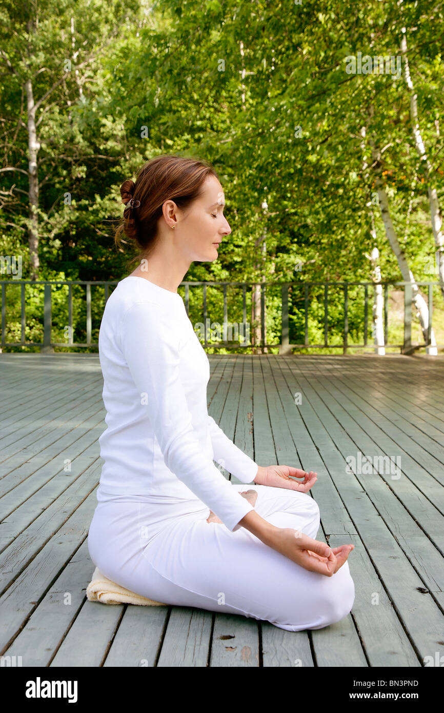 Woman sitting in lotus position on a deck, side view Stock Photo - Alamy