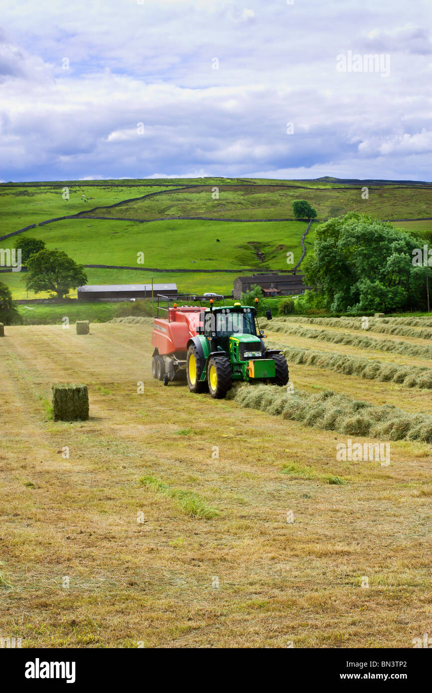 Working tractor in field making bales from cut grass / hay Stock Photo ...
