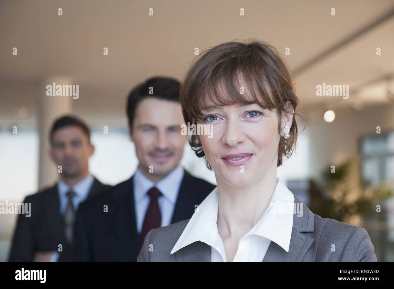 Business woman smiling at camera, two business men behind Stock Photo ...
