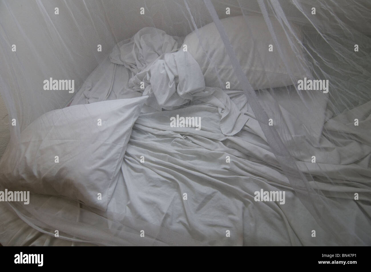 A messy bed with a draped mosquito net Stock Photo - Alamy