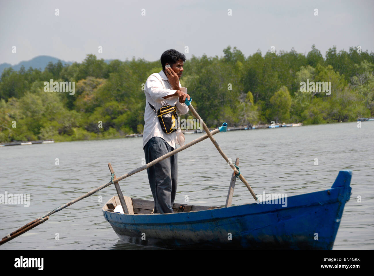 Local man using a mobile phone while rowing his boat, southern Thailand ...