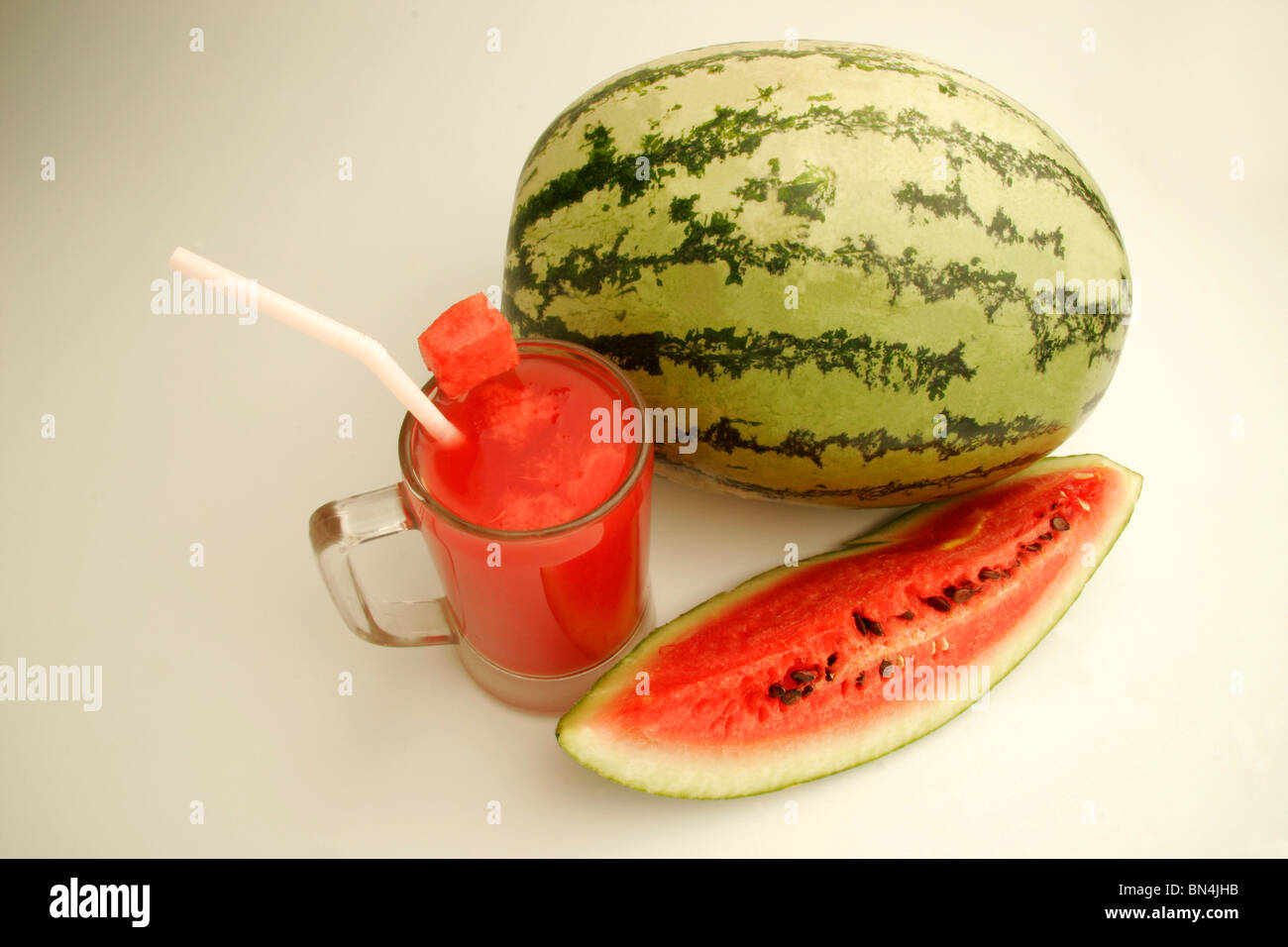 One full watermelon with glass of melon juice and cut slice showing red ...