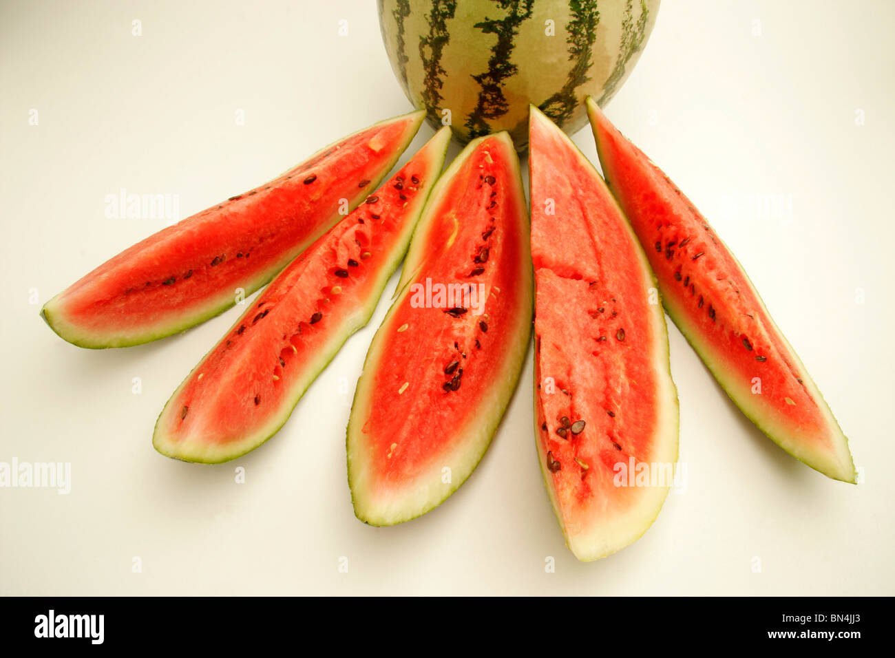 One full watermelon with five cut slices showing watery red pulp and ...