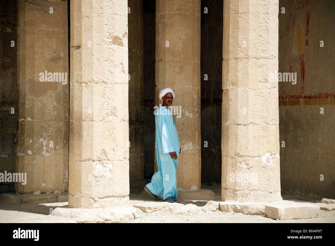 An egyptian man in a blue galabia walking by the columns of the ...