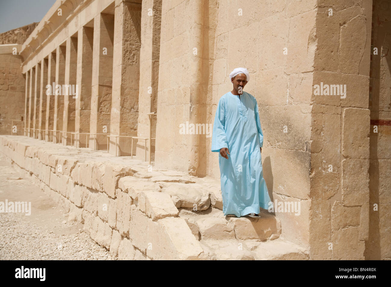 An egyptian man in a blue galabia walking by the columns of the ...