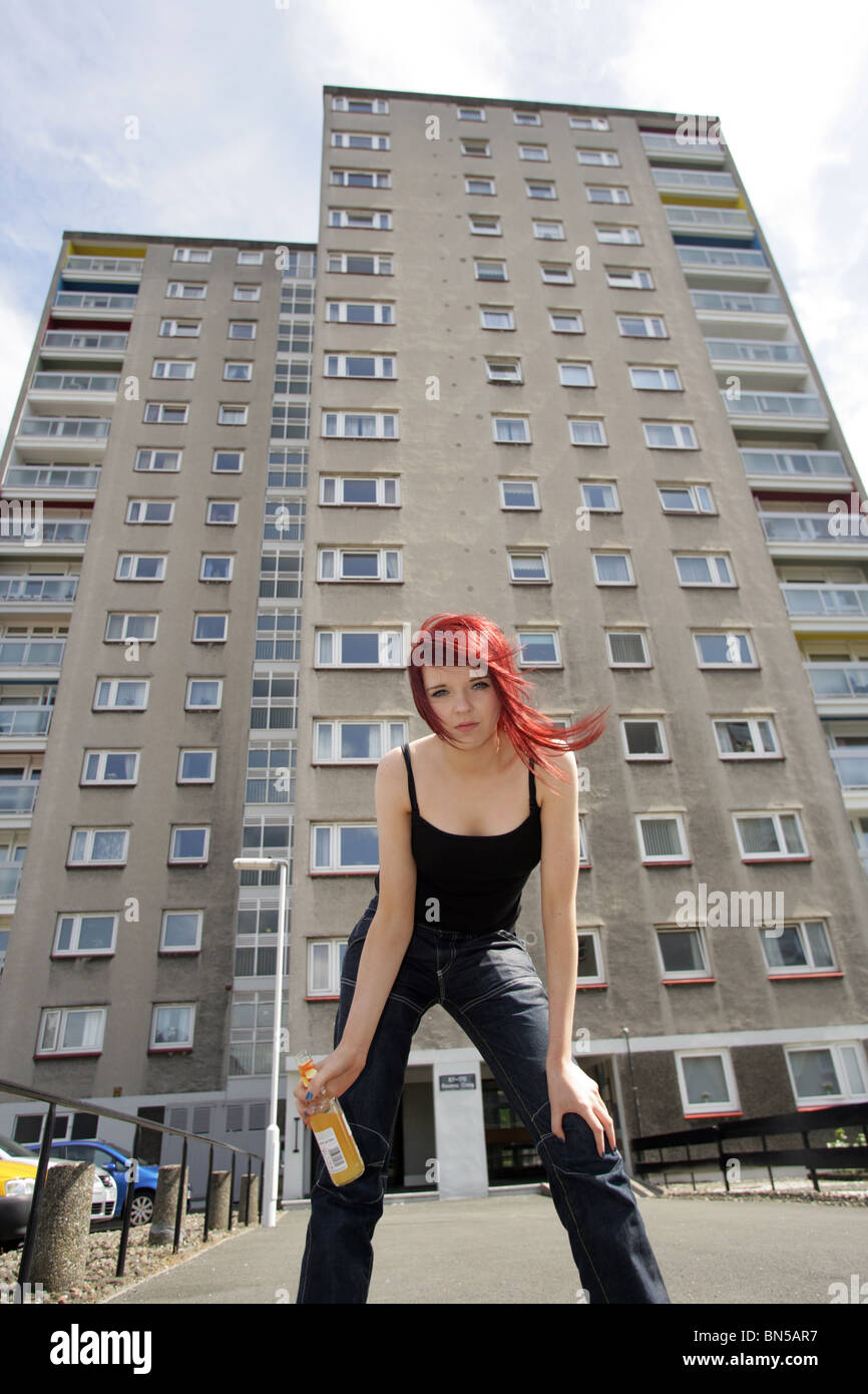 Teenage girl drinking from a bottle of alcohol outside a block of flats ...