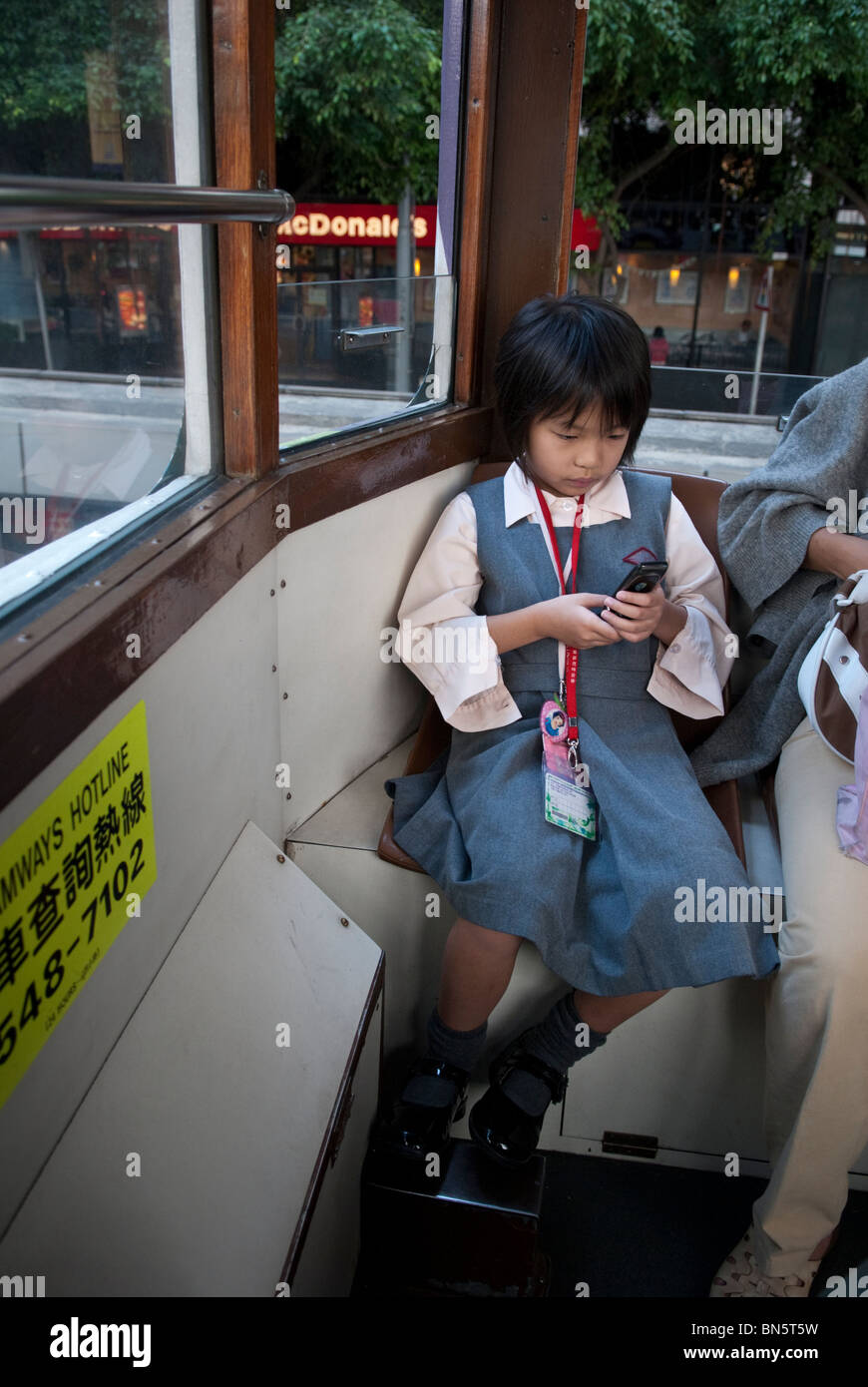 Hong Kong, 13 November, 2007 Young girl in school uniform sending text message in Hong Kong tram ...