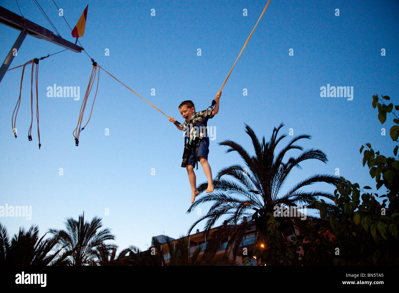 A young boy bounces high on a fairground Bungee Jump against the blue ...