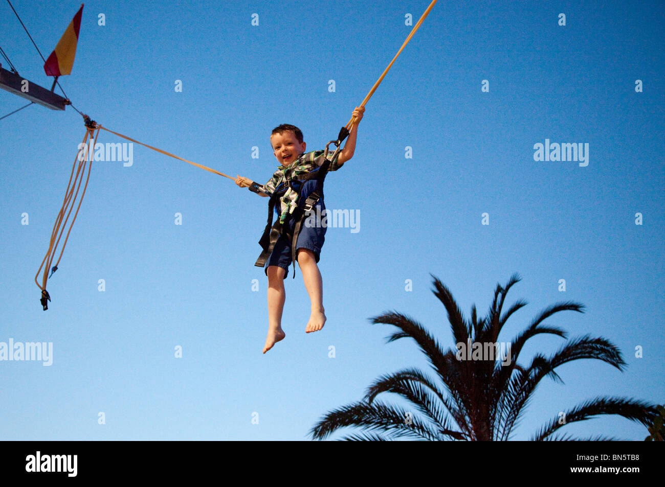 A young boy bounces high on a fairground Bungee Jump against the blue ...