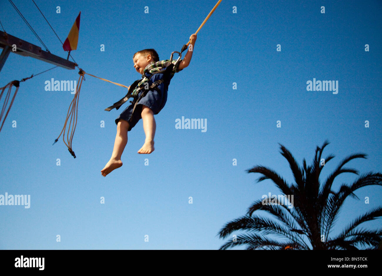 A young boy bounces high on a fairground Bungee Jump against the blue ...