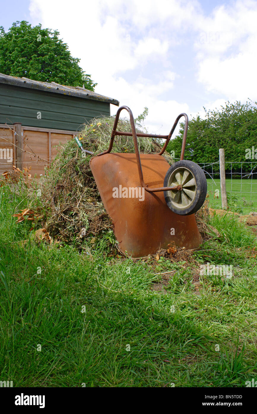 wheel barrow leaning against a pile of garden waste Stock Photo - Alamy