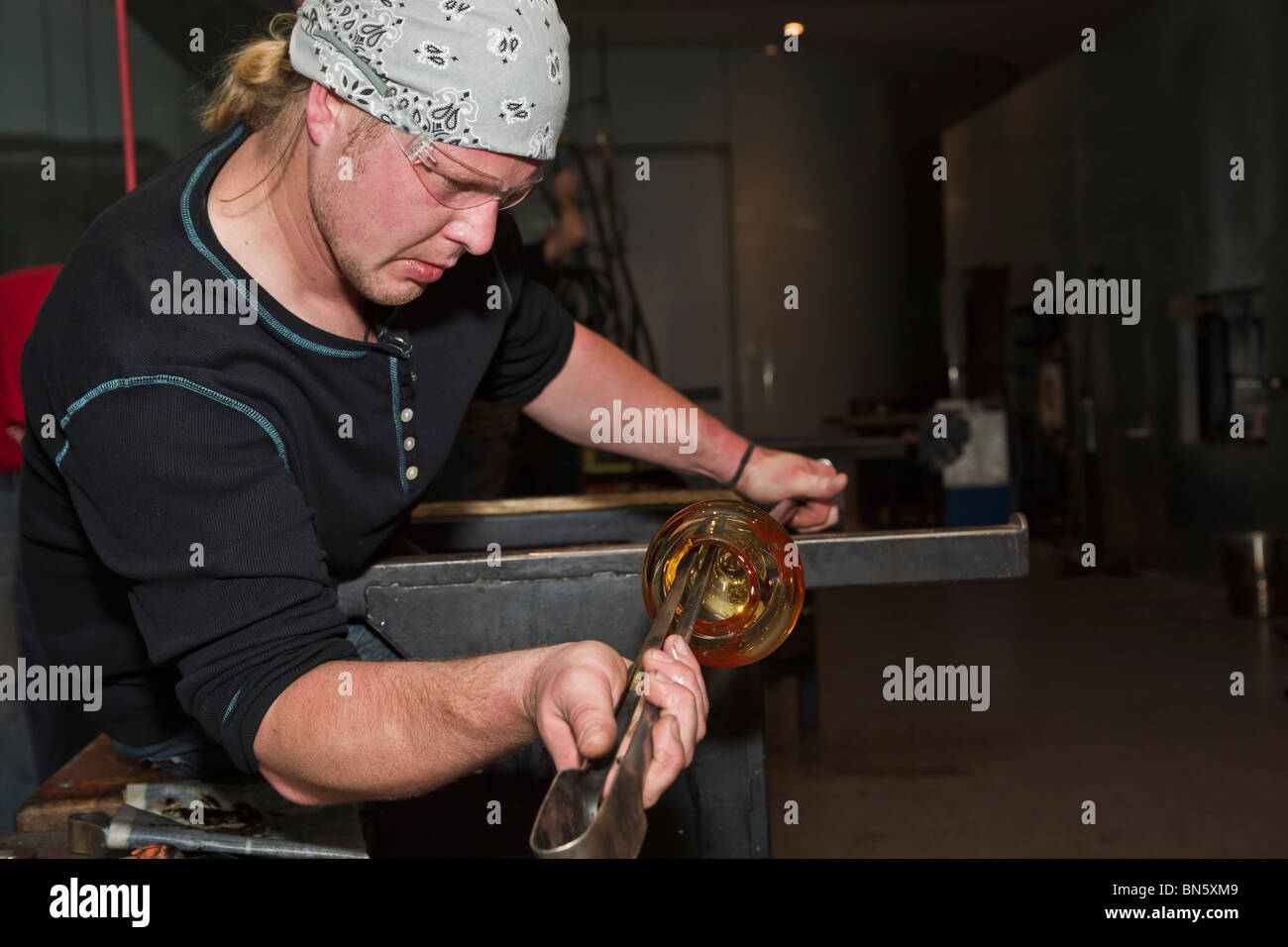 A young glassblower making forming hot glass mold using tools in from ...