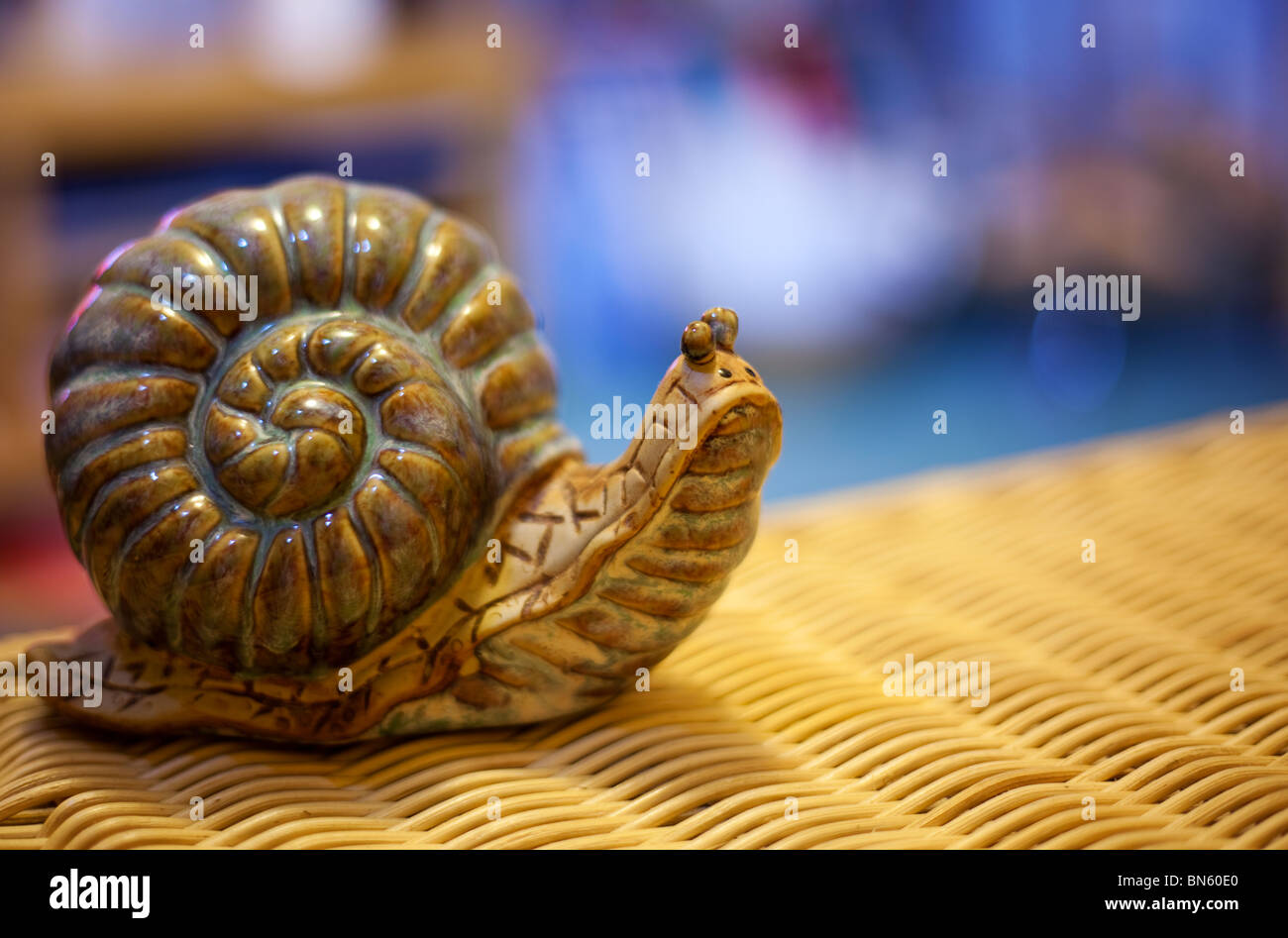 Small Snail macro sculpture against blue background on a rattan surface ...
