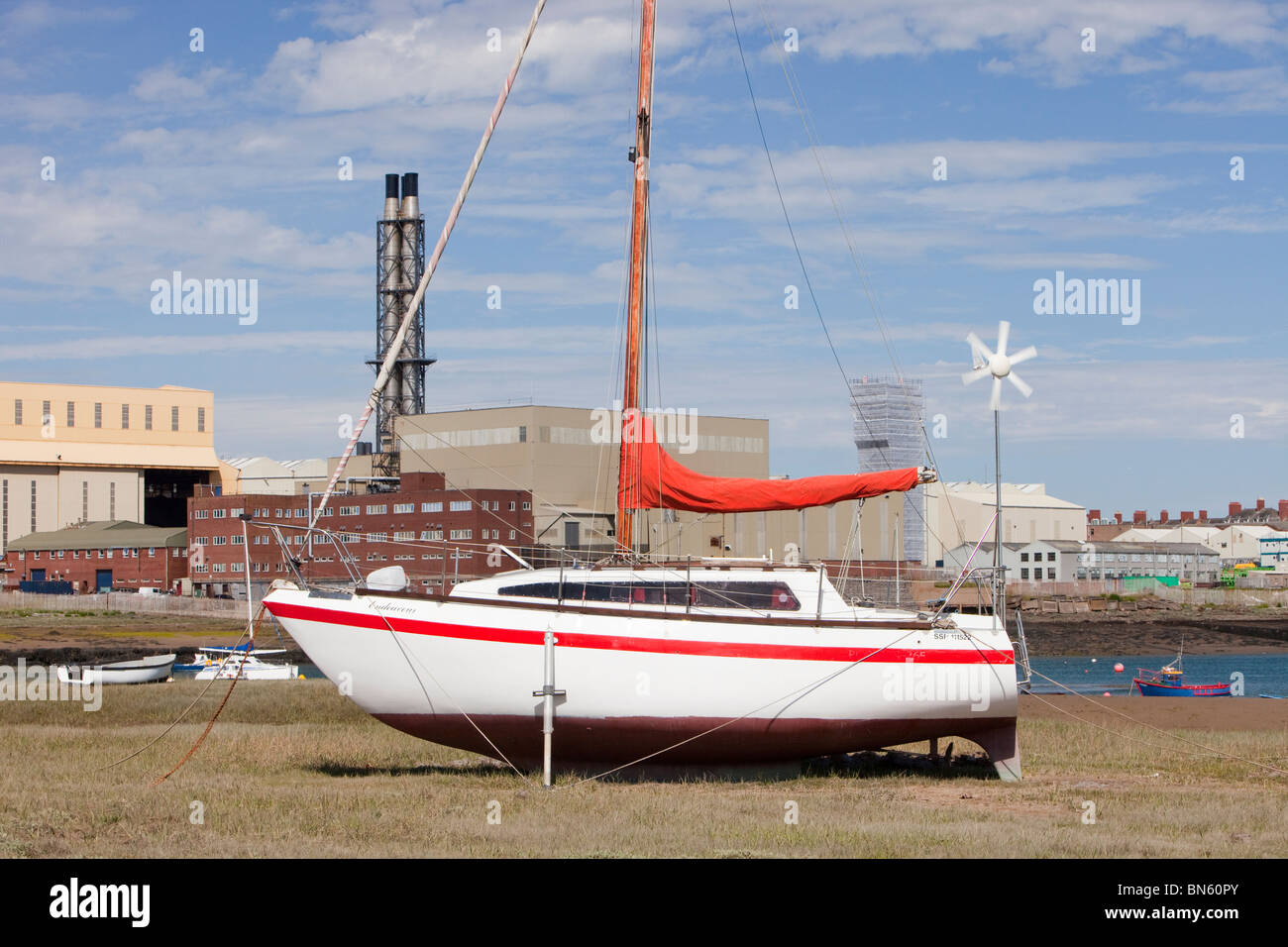 A yacht with a small wind turbine in front of the BAE Systems ...