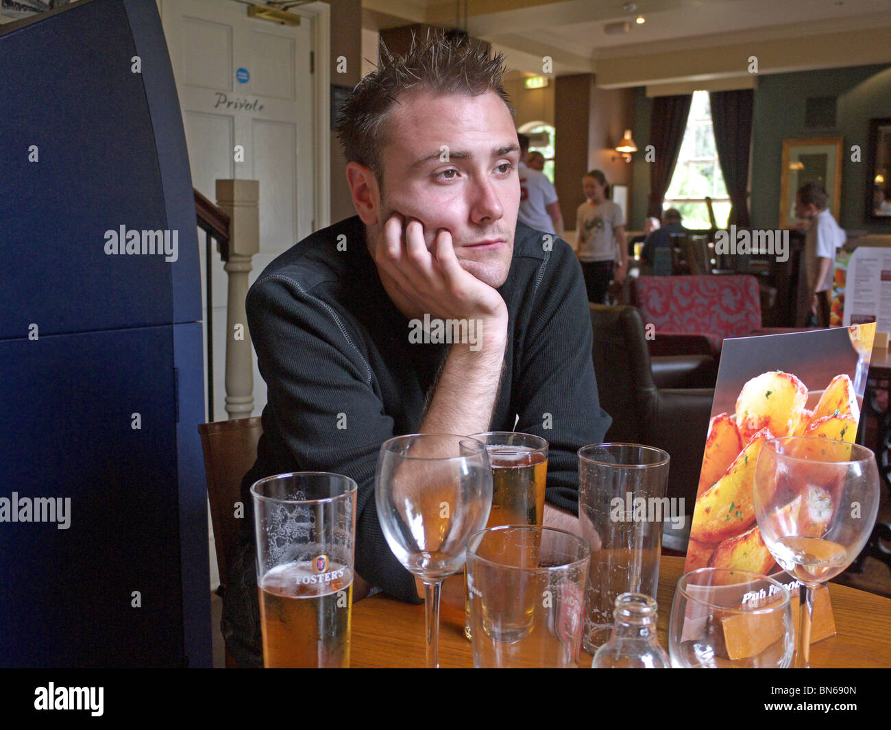 A young man leaning on his hand sitting in a pub looking thoughtful ...