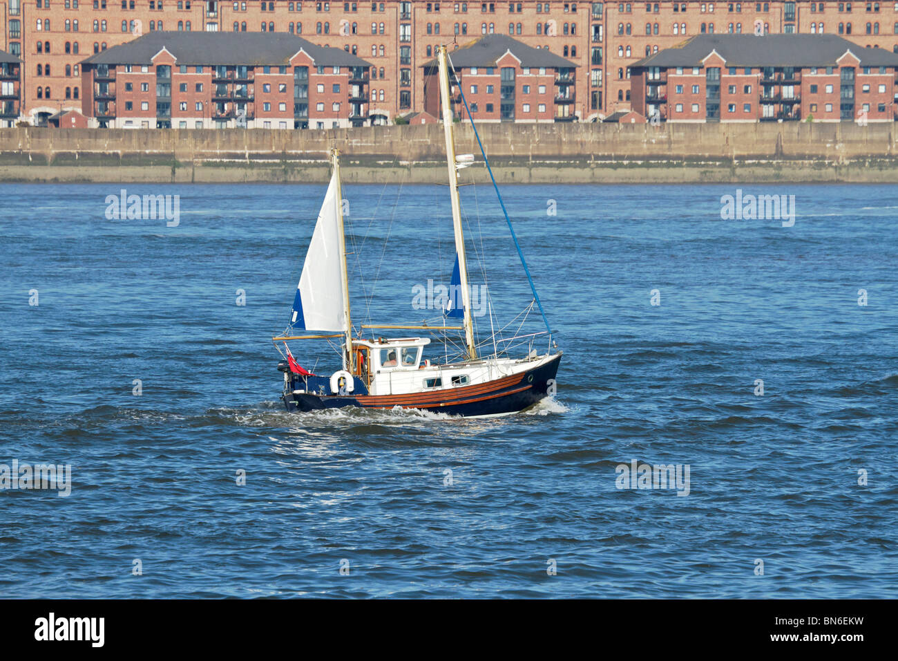 Small sailing boat heading up river Mersey on a bright sunny evening ...