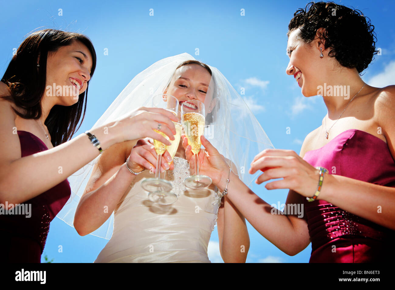 Bride with two bridesmaids gives a cheers with filled champagne glasses ...