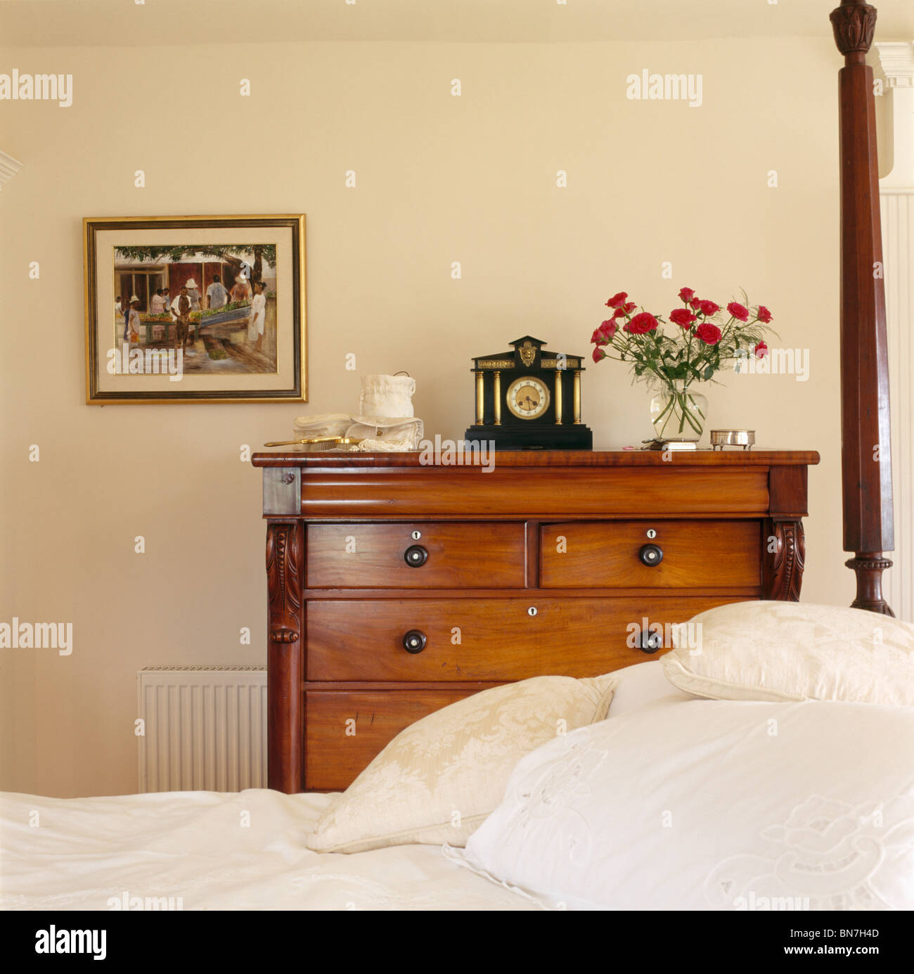 Clock on antique chest-of-drawers beside bed with white linen in white ...