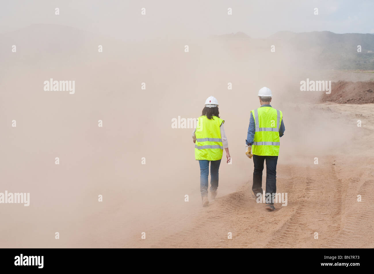 Construction workers walking in cloud of dust Stock Photo - Alamy