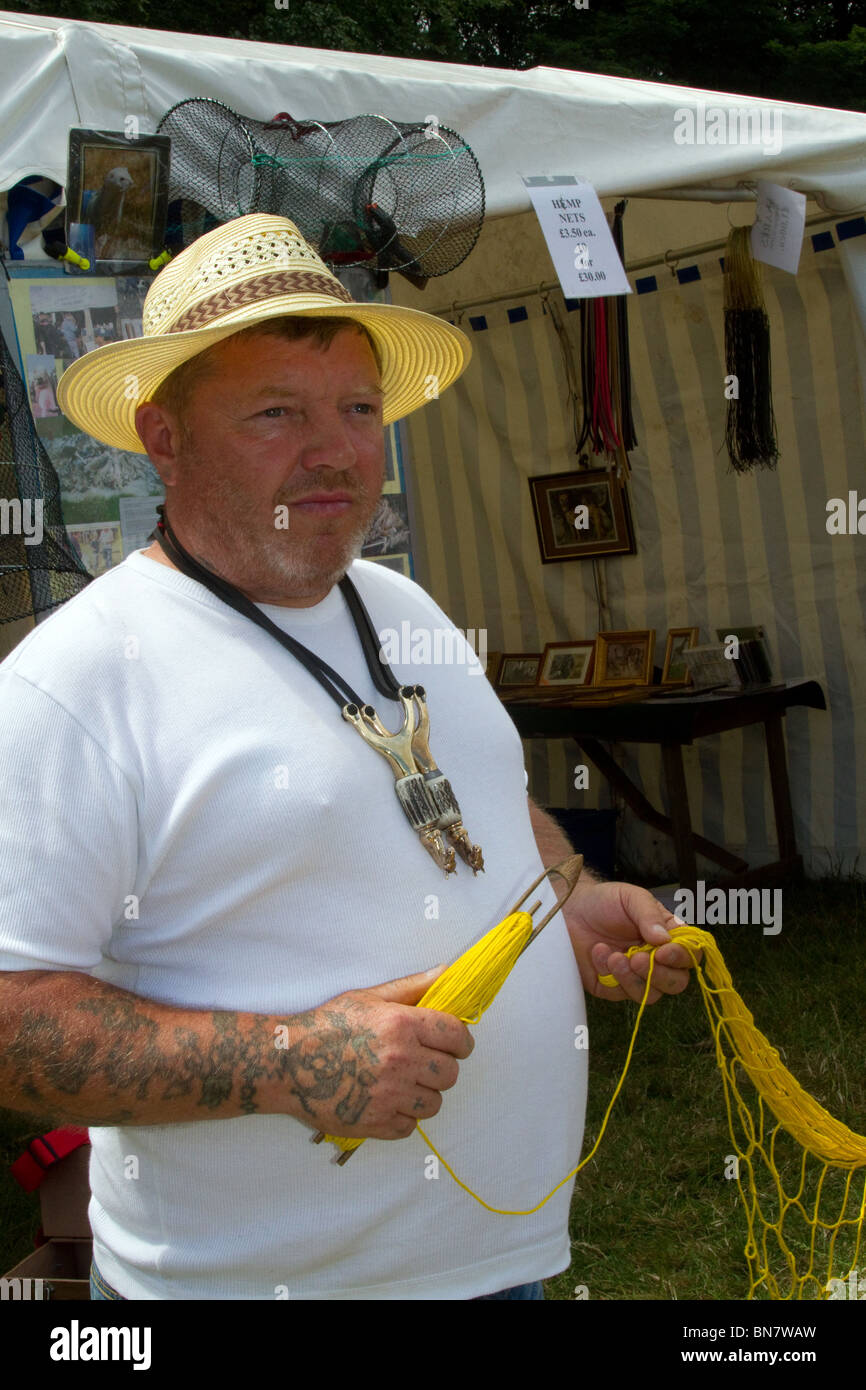Stallholder with netting bobbin, and wearing hand-made catapults around ...
