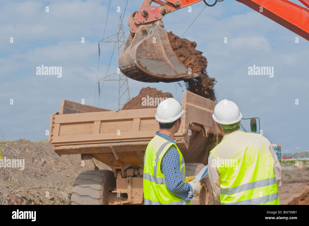Hispanic construction workers watching dirt falling into dump truck ...