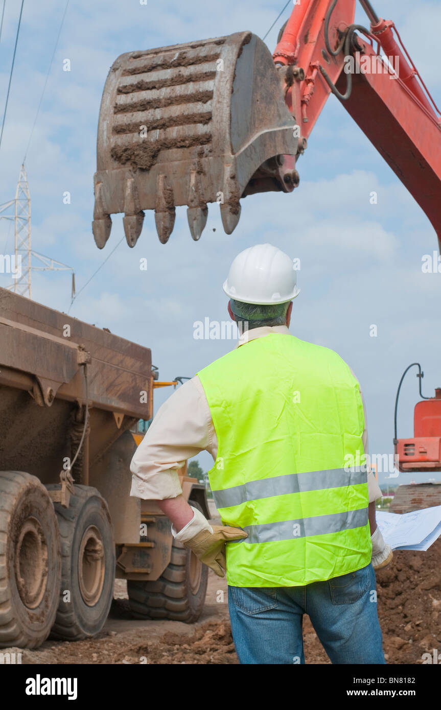 Hispanic construction worker watching backhoe Stock Photo - Alamy