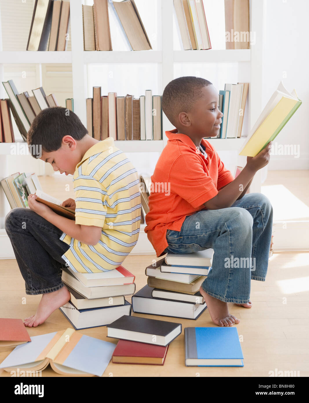 Boys sitting on stacks of books and reading Stock Photo - Alamy