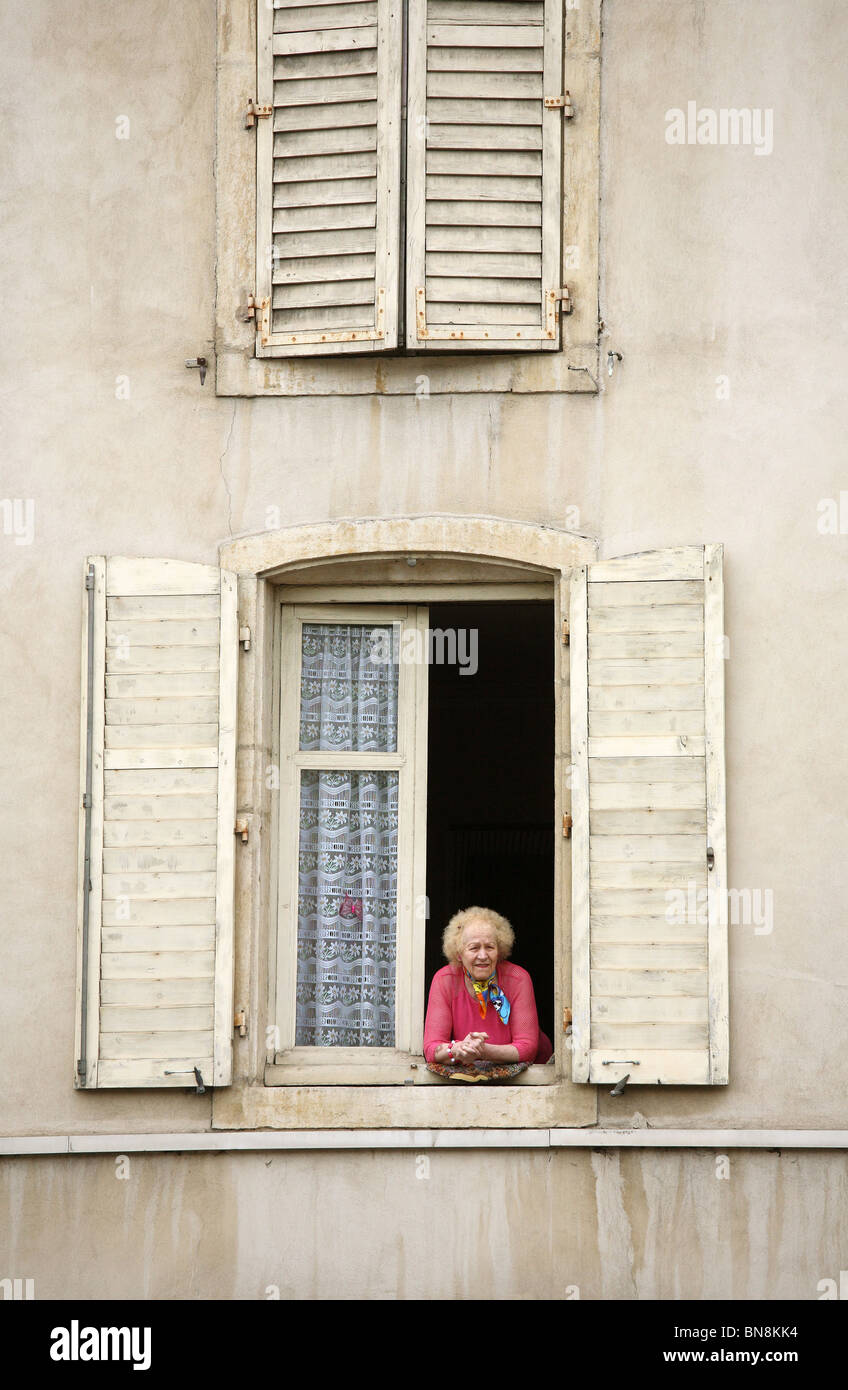 An elderly woman looking out of the window of an old apartment building ...