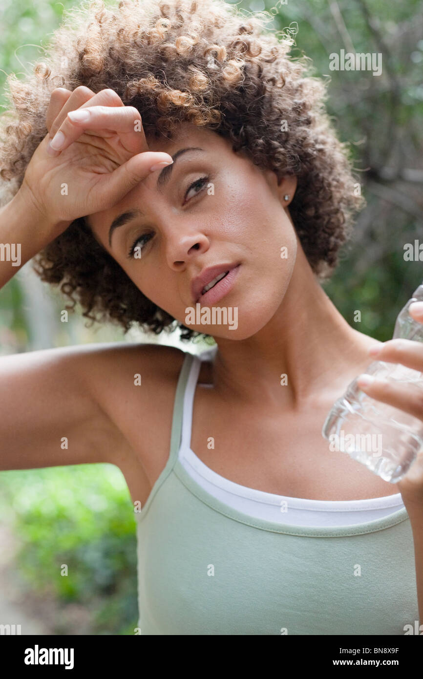 Mixed race woman wiping forehead and drinking water Stock Photo - Alamy