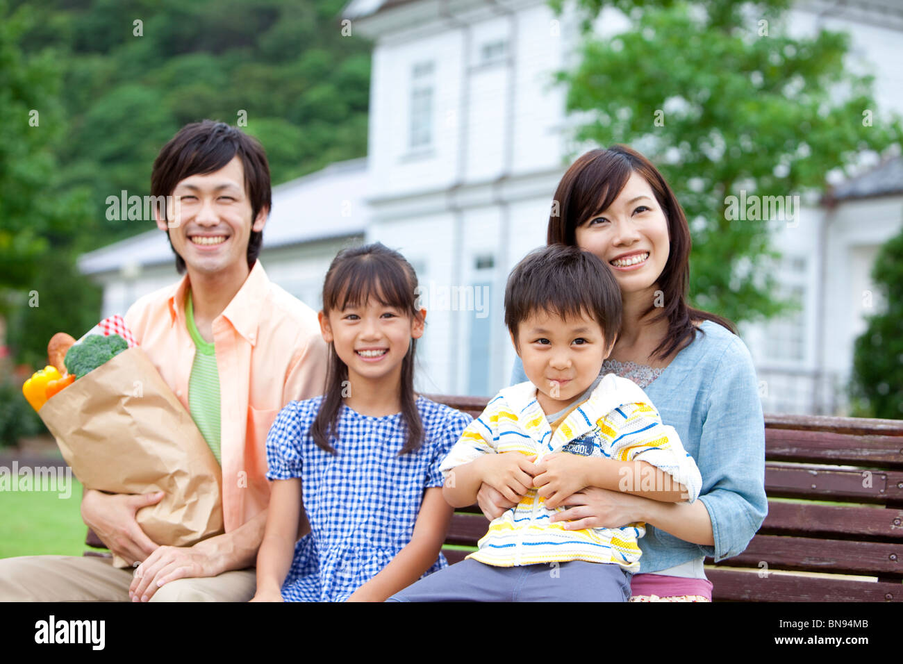 Portrait of family sitting on bench smiling Stock Photo - Alamy