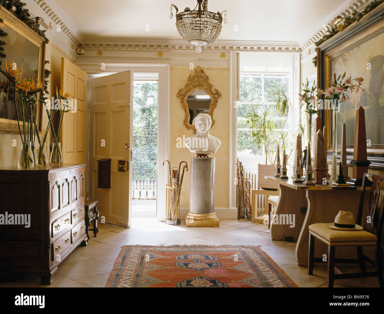 Classical bust on column in large country hall with antique furniture ...