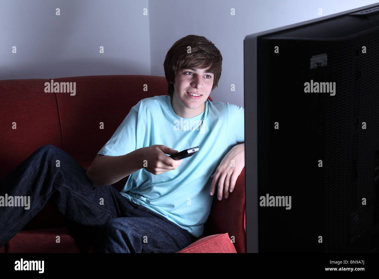 Young male watching tv alone holding a remote control Stock Photo - Alamy