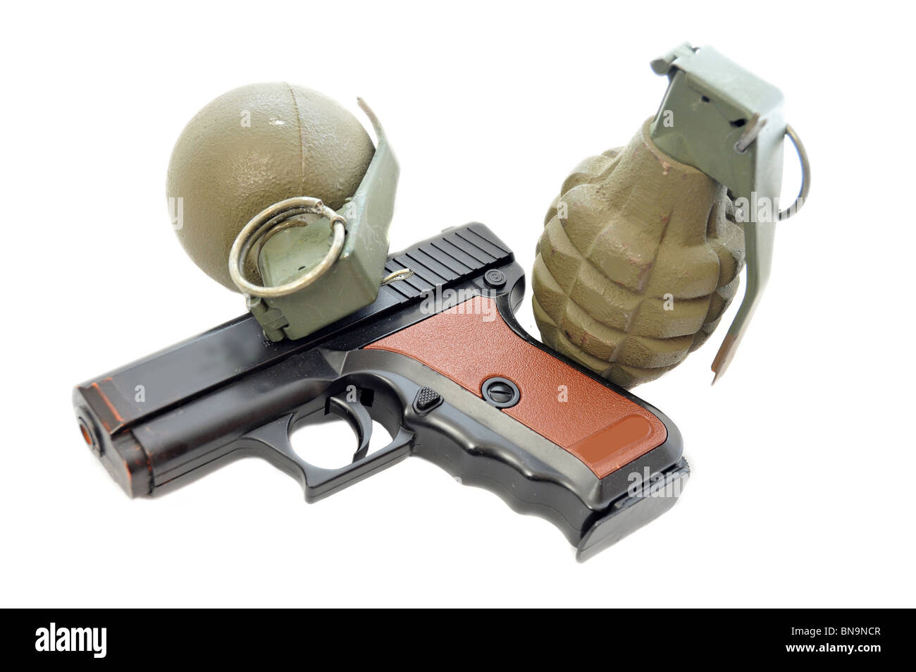 A plastic pistol and two metal green hand grenades isolated on white ...
