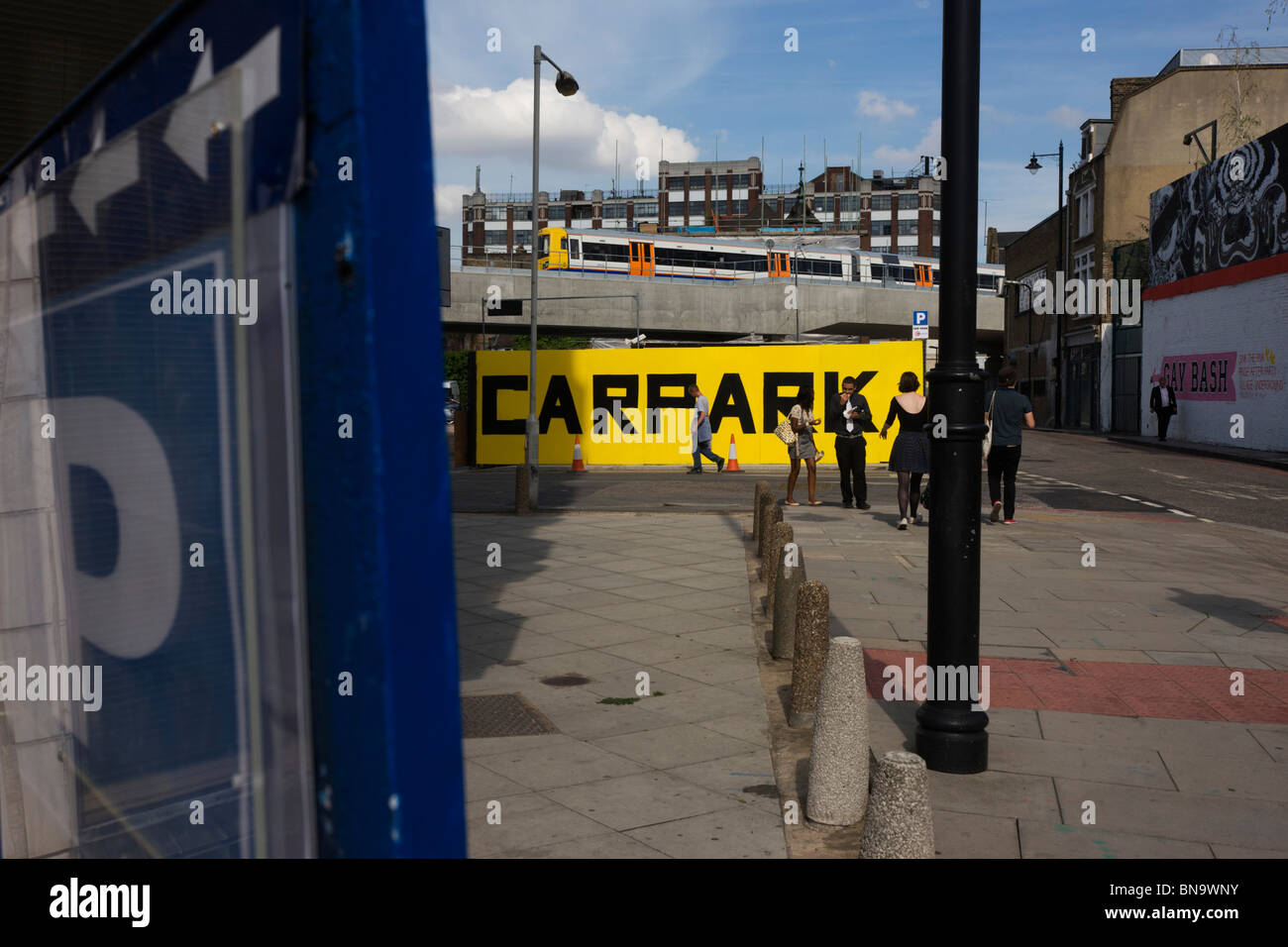 Pedestrians walk past large yellow car park sign on street in East ...