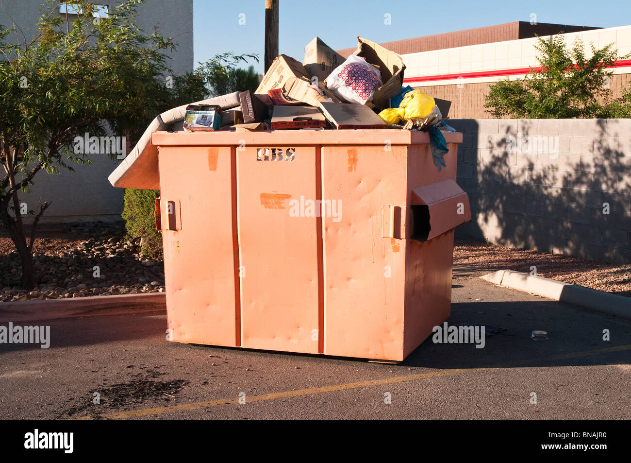 An orange dumpster is full of various types of trash and ready to be ...