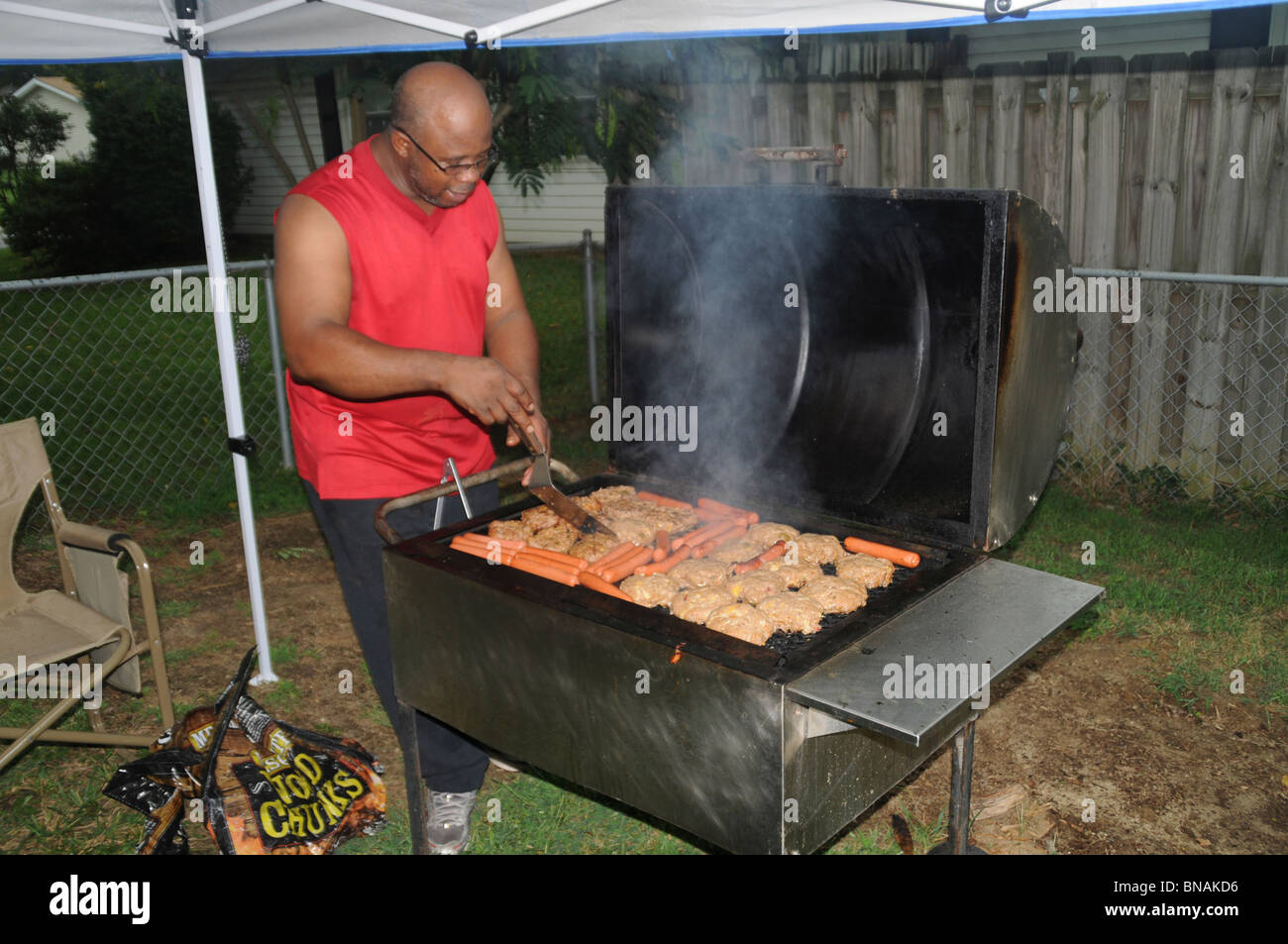 man grilling hamburgers and hot dogs on outside grill Stock Photo - Alamy