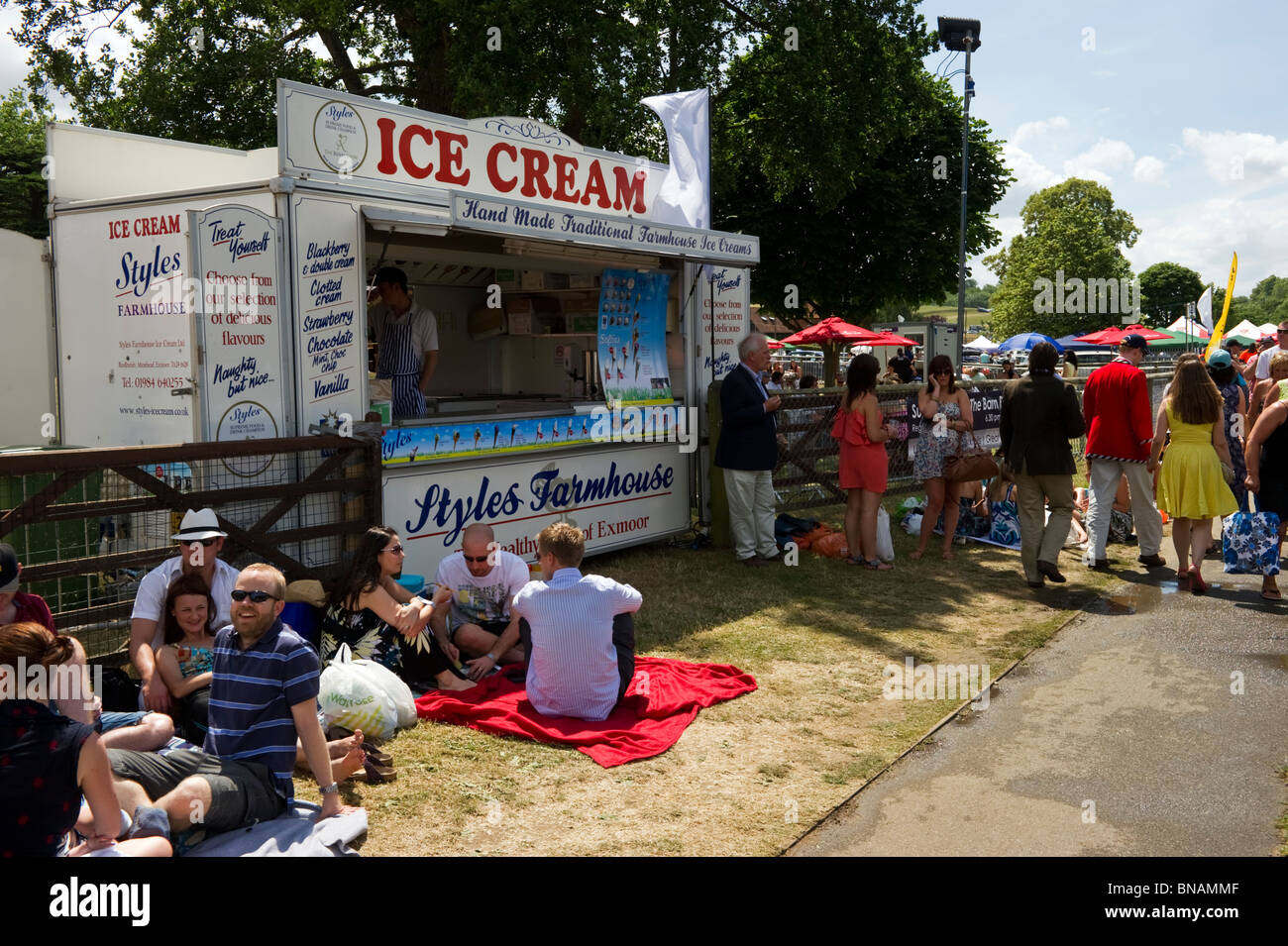 A crowd of people at an ice cream stand in sunshine on a hot sunny ...