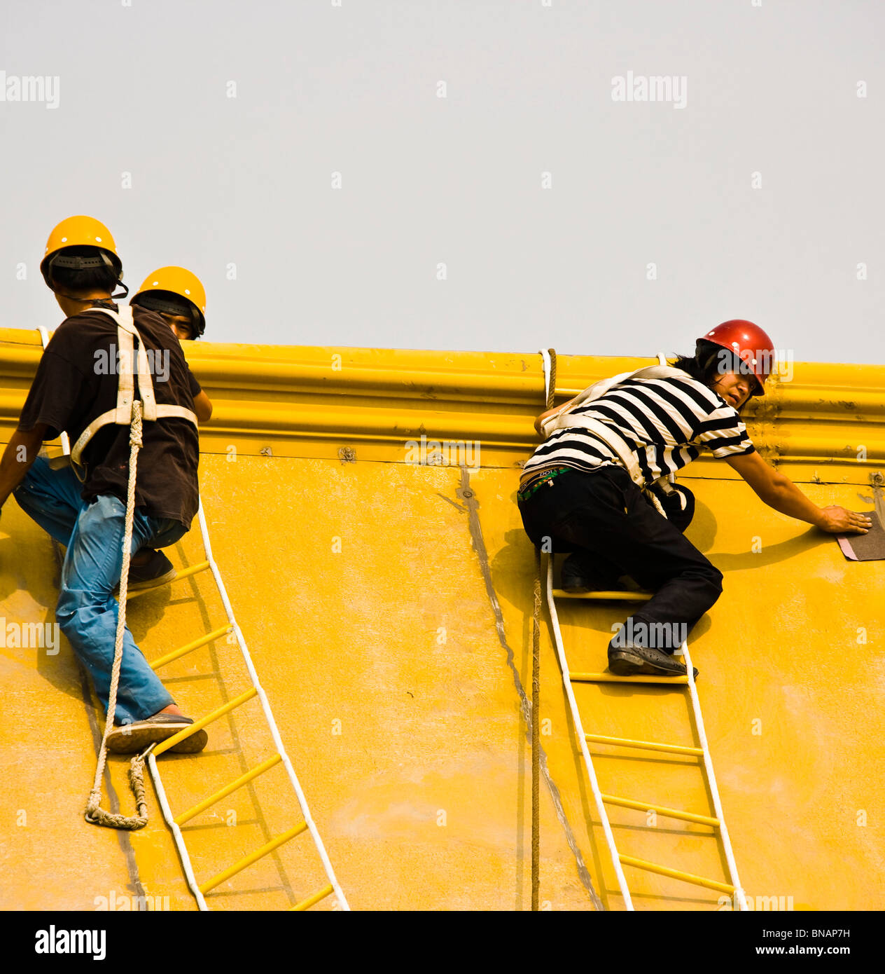 Workers using rope ladders to paint roof of a yellow building in ...