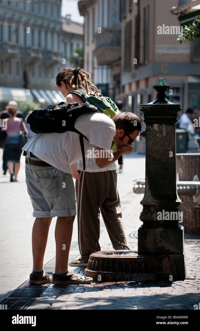 two men drinking at public water fountain in the centre of Monza Italy ...