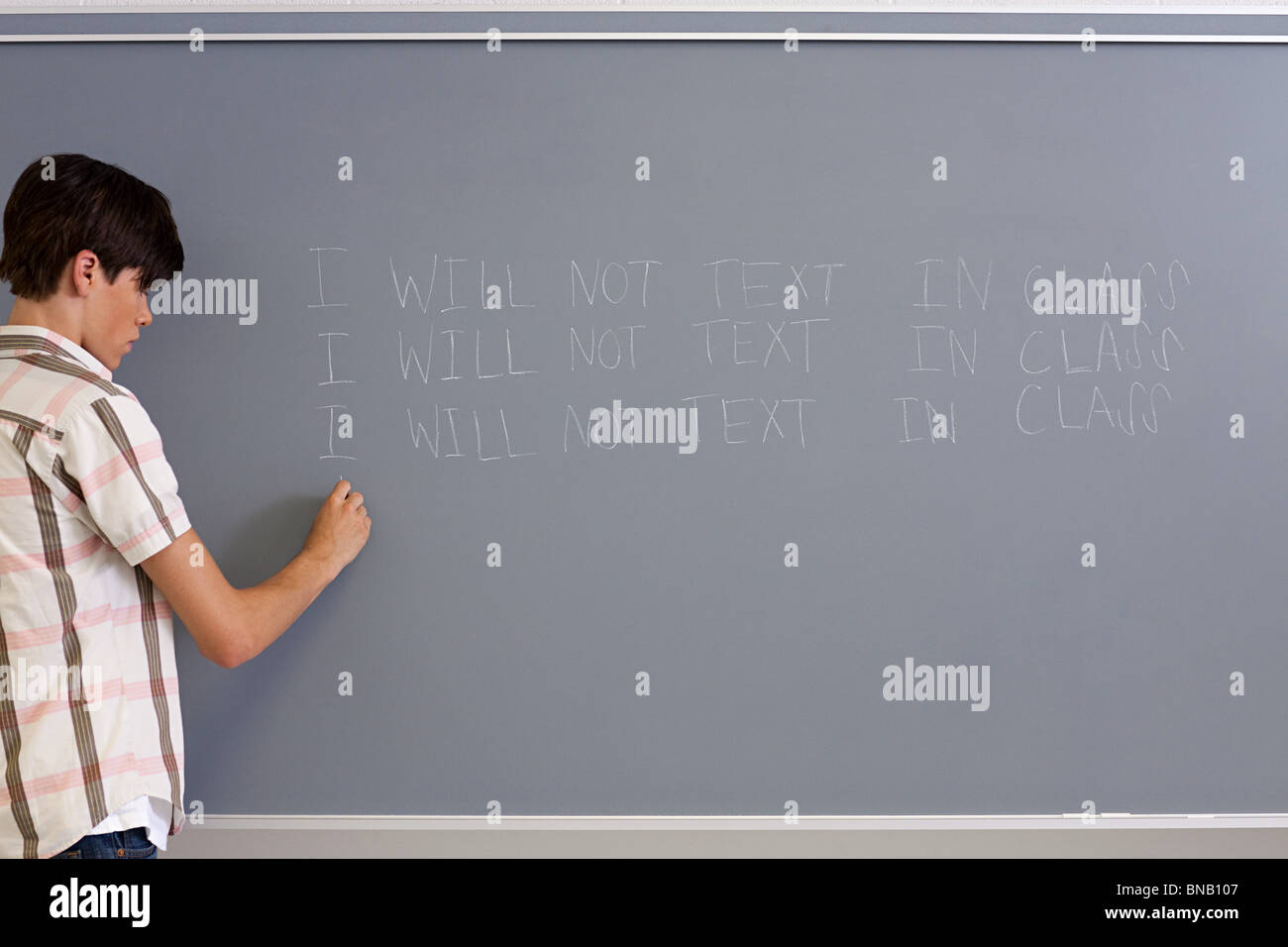 Male high school student writing lines on blackboard Stock Photo - Alamy
