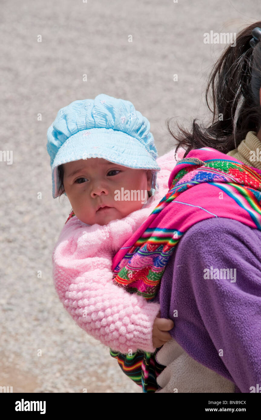 A young peruvian girl in ethnic dress carrying a baby on her back in ...