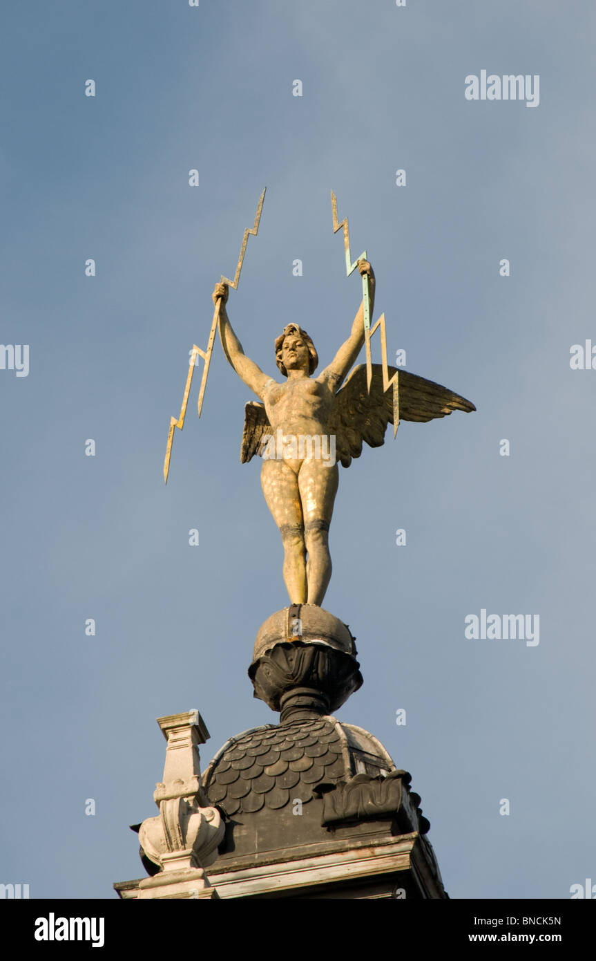 A winged statue holding lightning bolts on top of a building in Antwerp ...